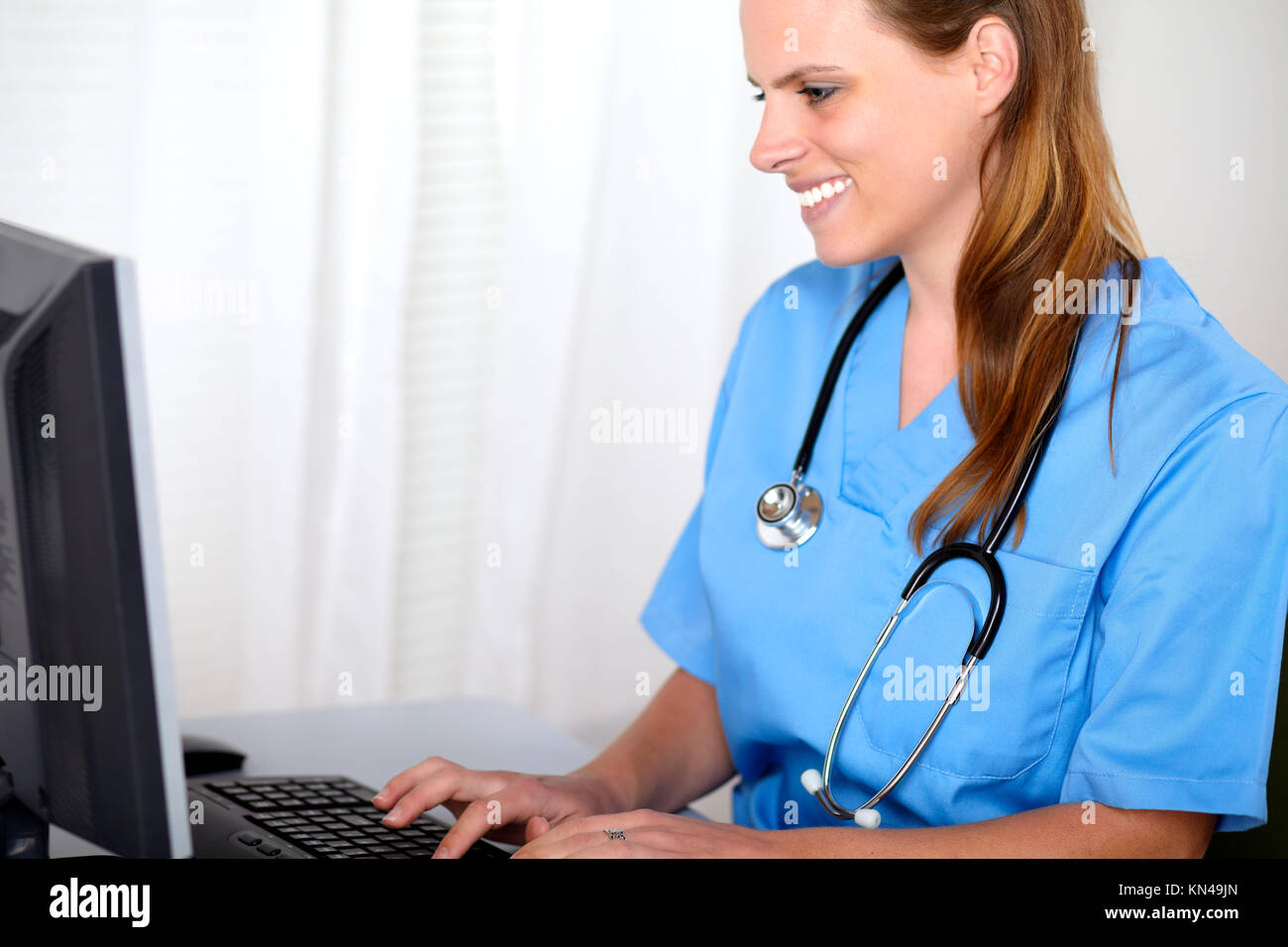 Portrait of a blonde friendly young nurse looking to computer screen at ...