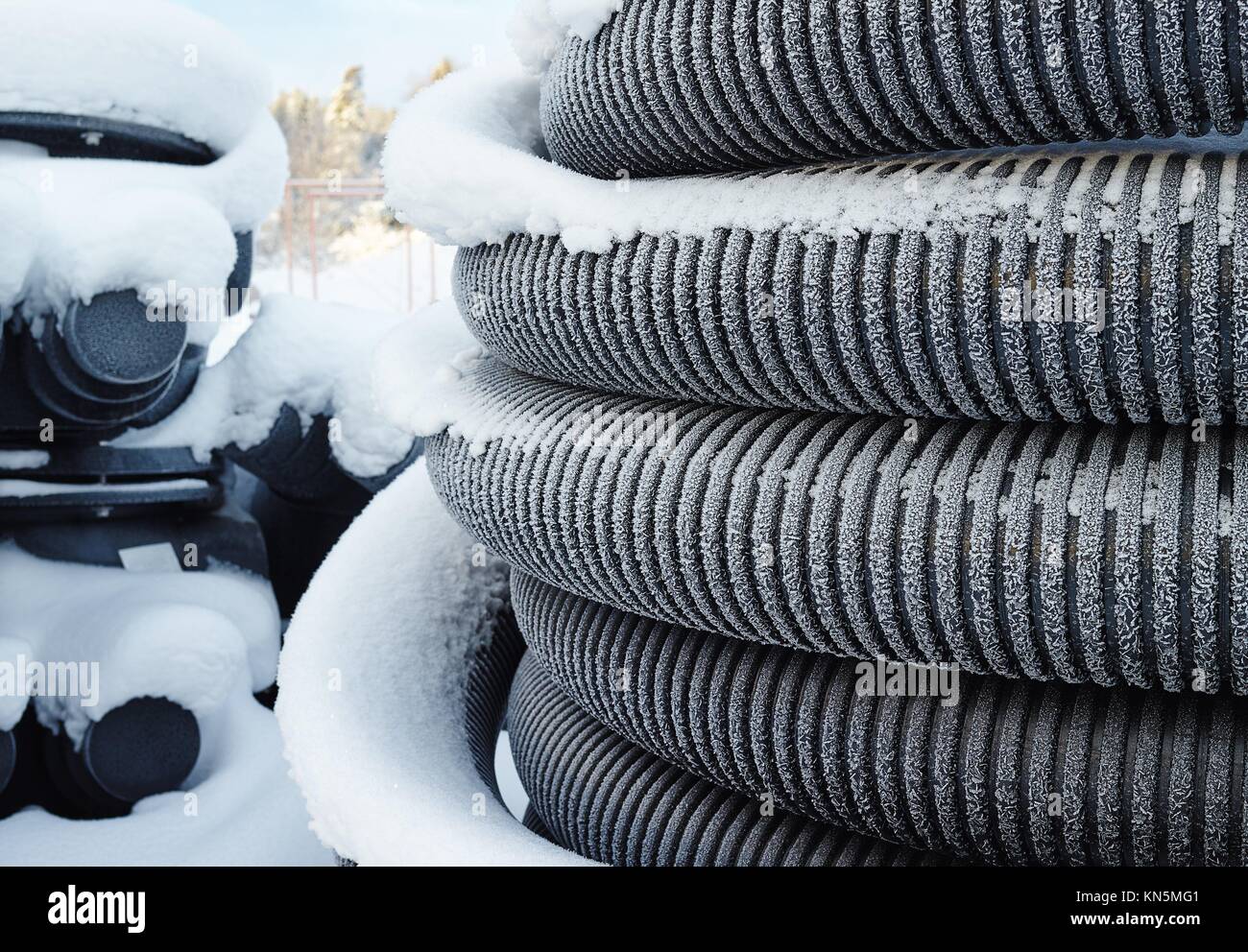Rolls of plastic pipes or tubes stacked outdoor yard, snowy and cold ...