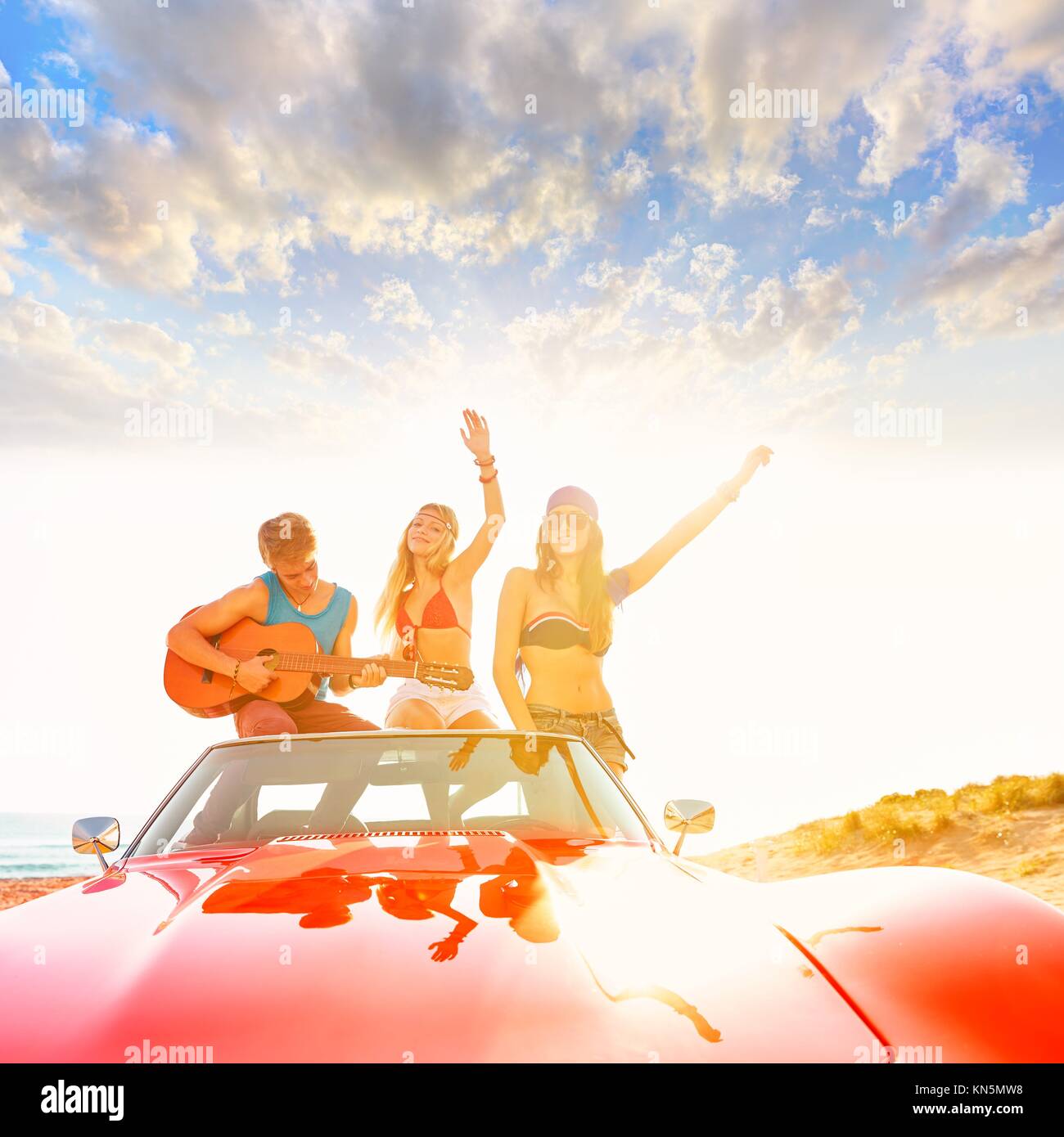 young group having fun on the beach playing guitar and dancing in a ...