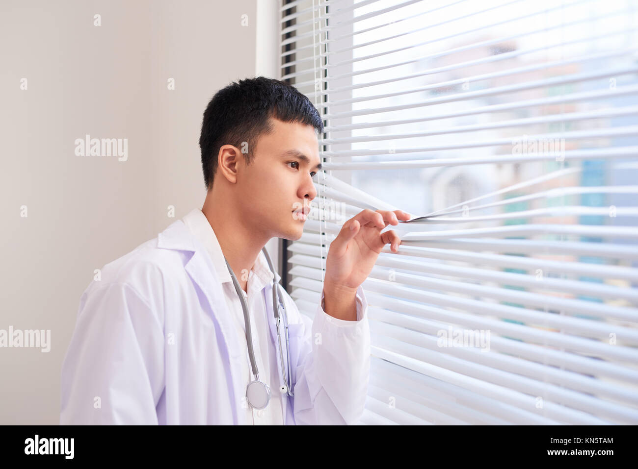 Young male asian doctor looking out of the window at hospital Stock ...