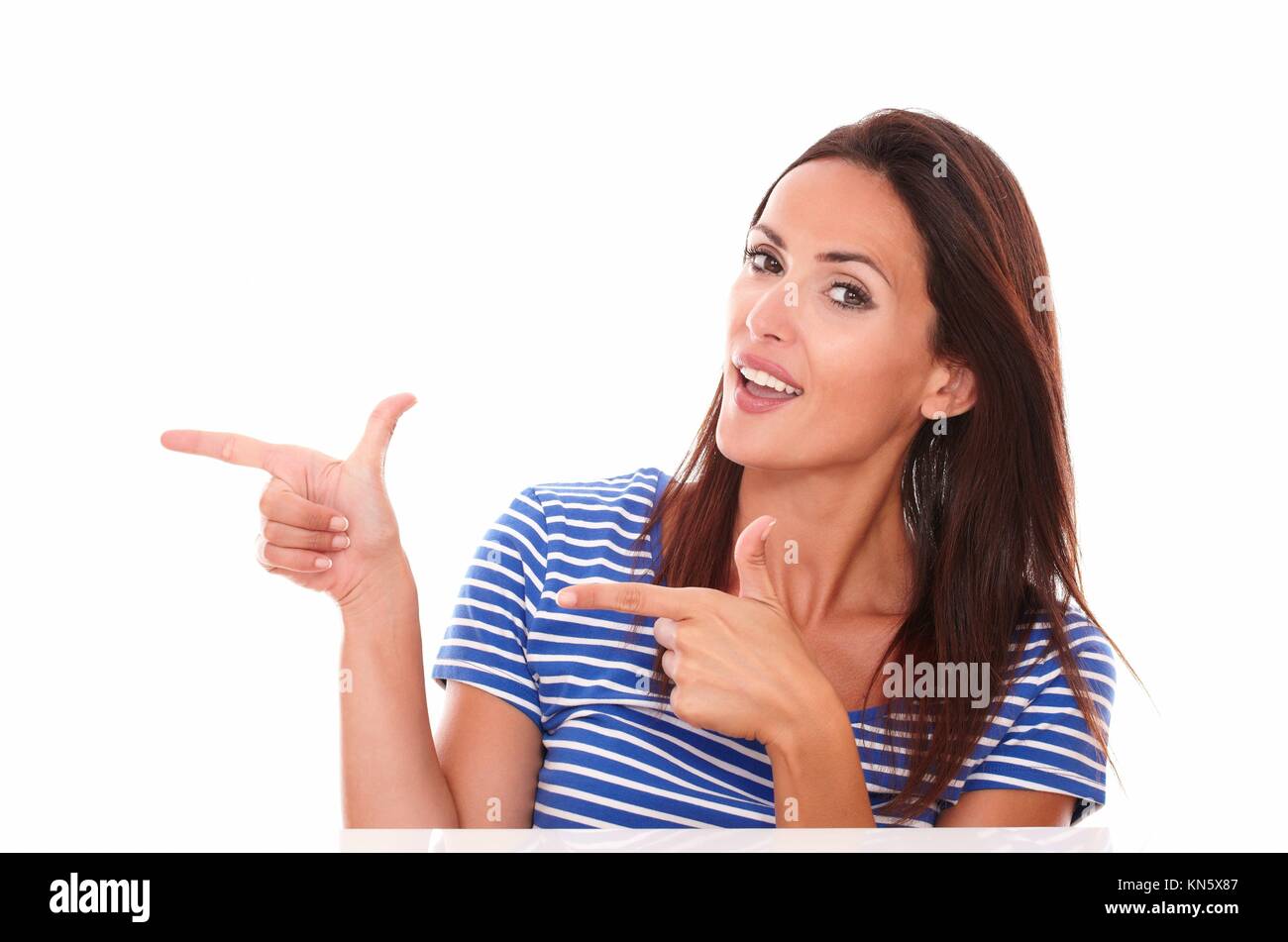 Attractive woman pointing to her right and smiling in white background ...