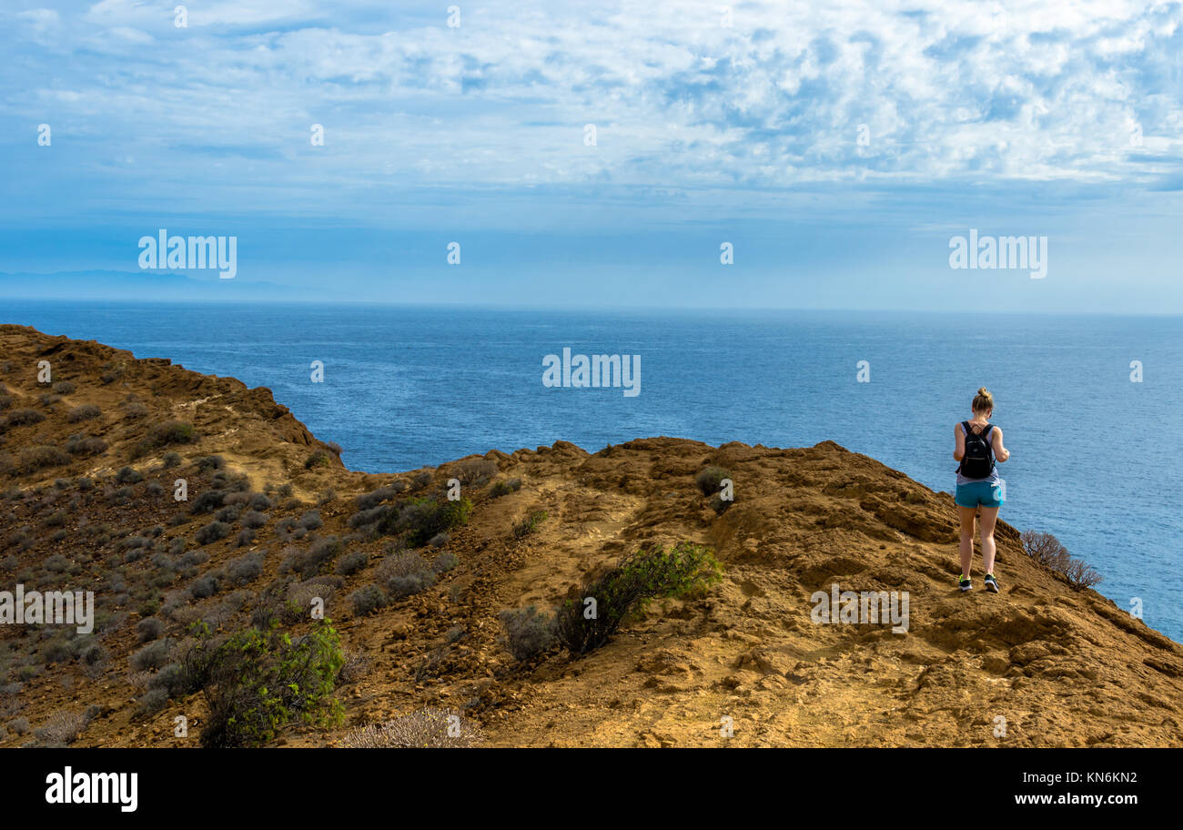 A young woman in a small backpack walks by the Atlantic Ocean in ...