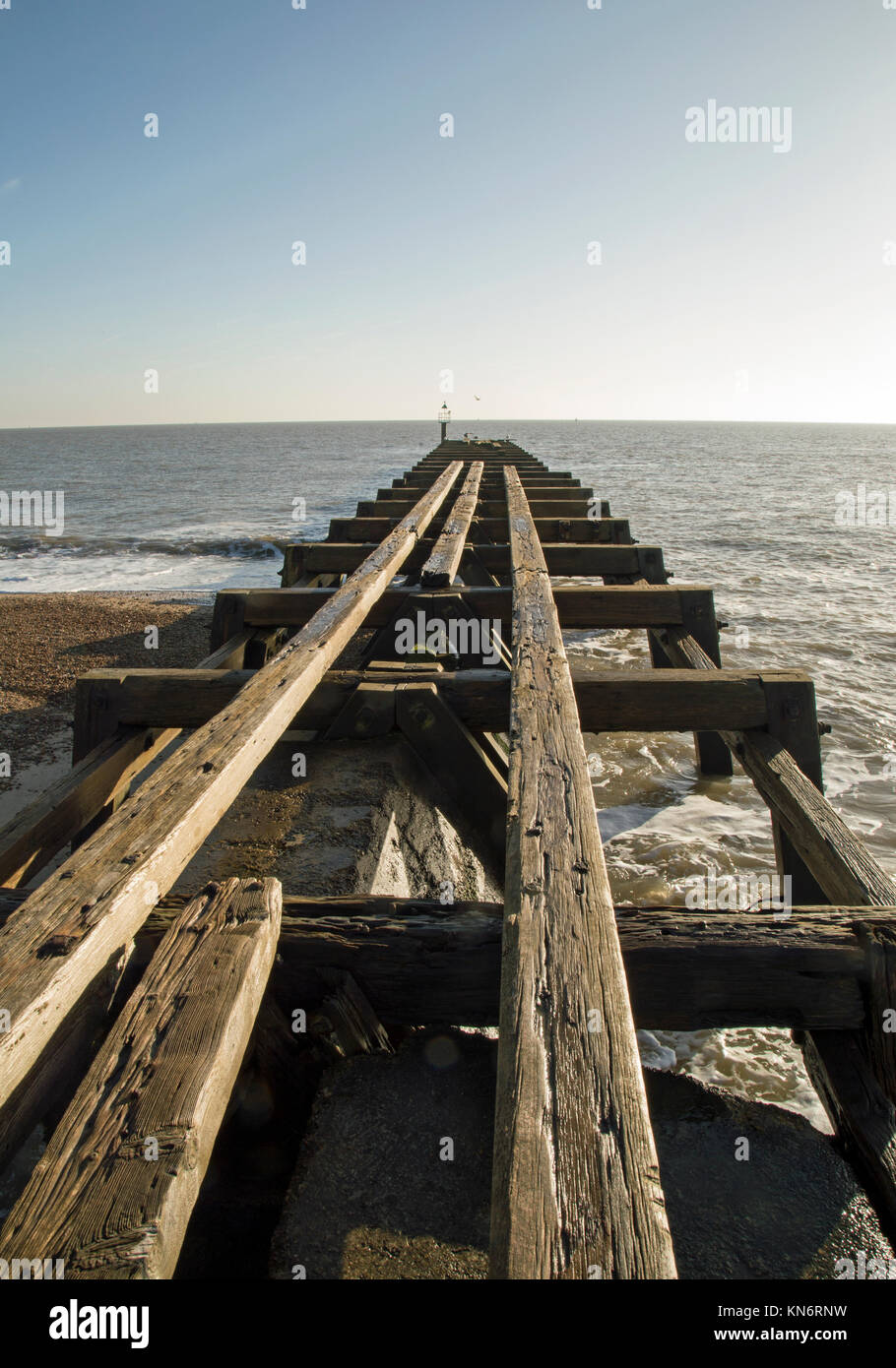 A derelict and weathered jetty leading out to sea shot in portrait ...