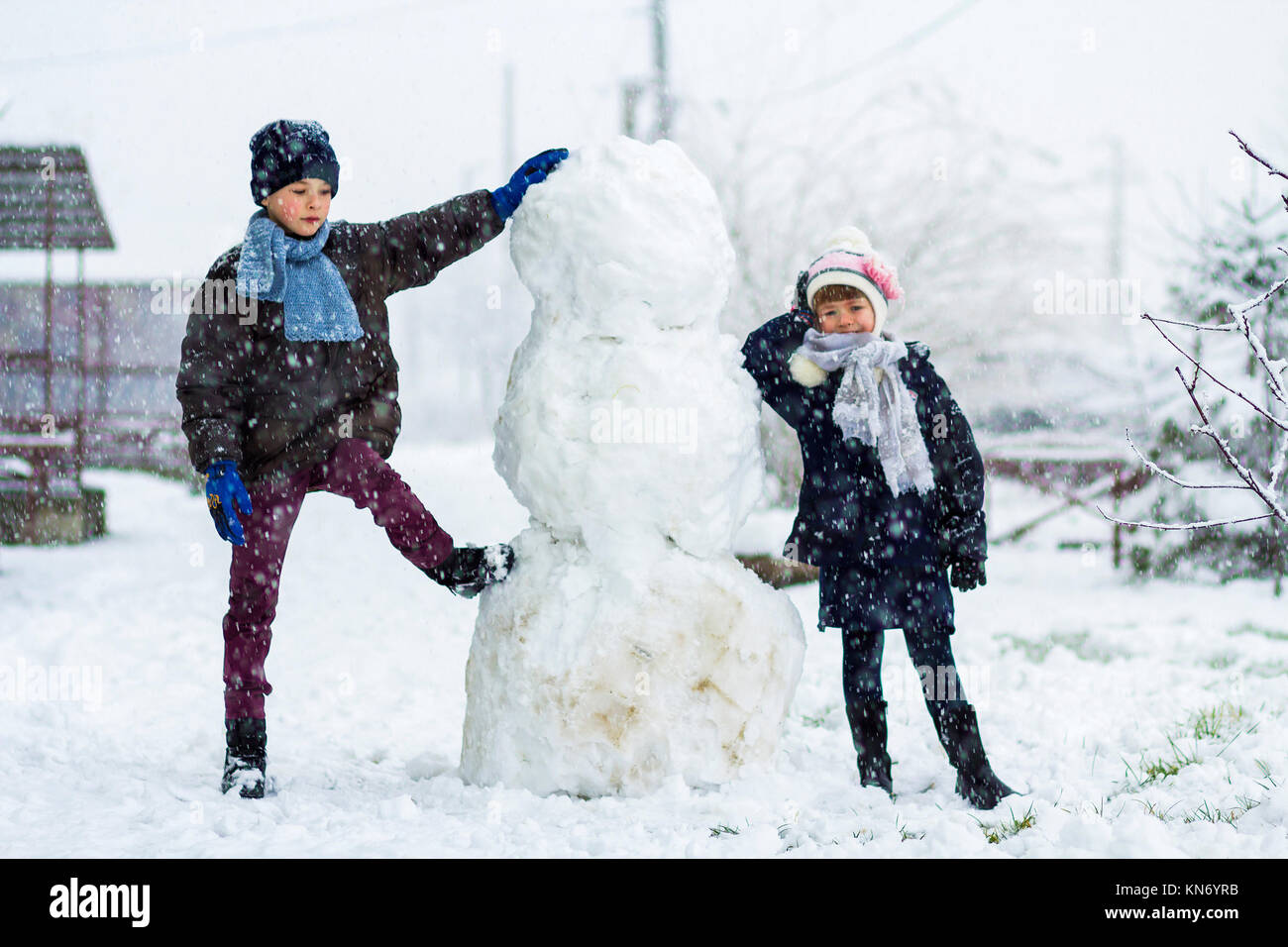 Children boy and girl outdoors in snowy winter are making a big snowman ...