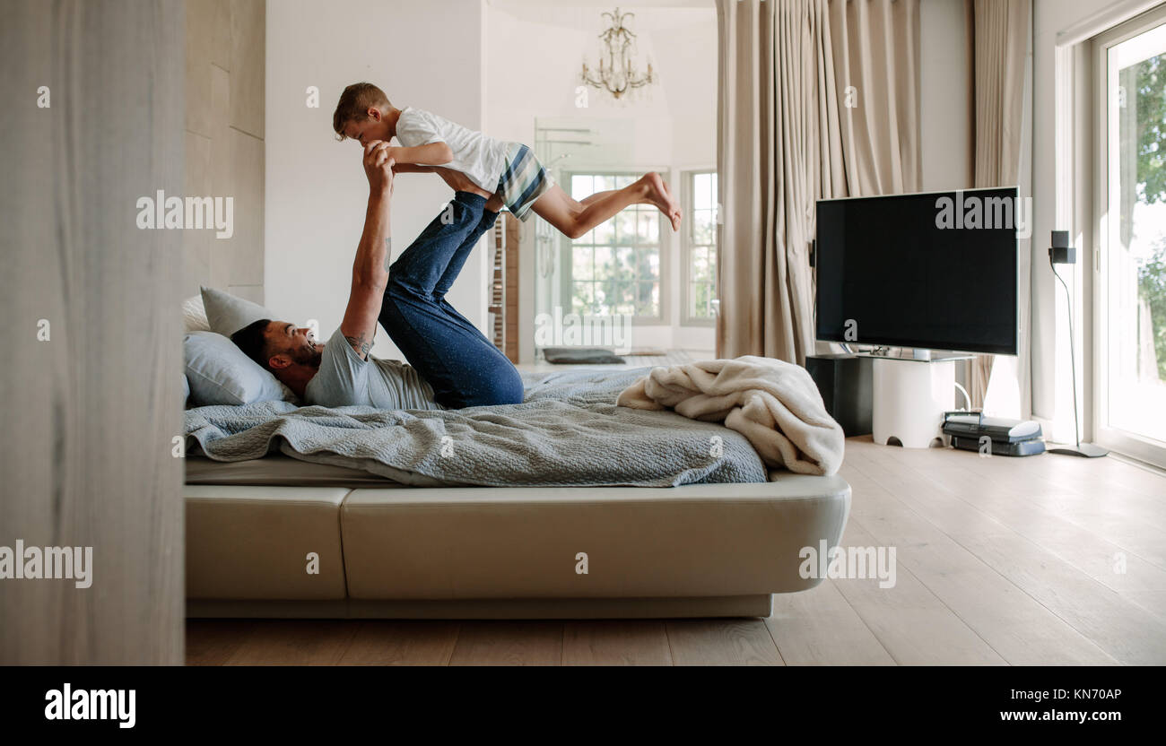 Father playing in bed with son. Man holding a little boy on his legs in ...