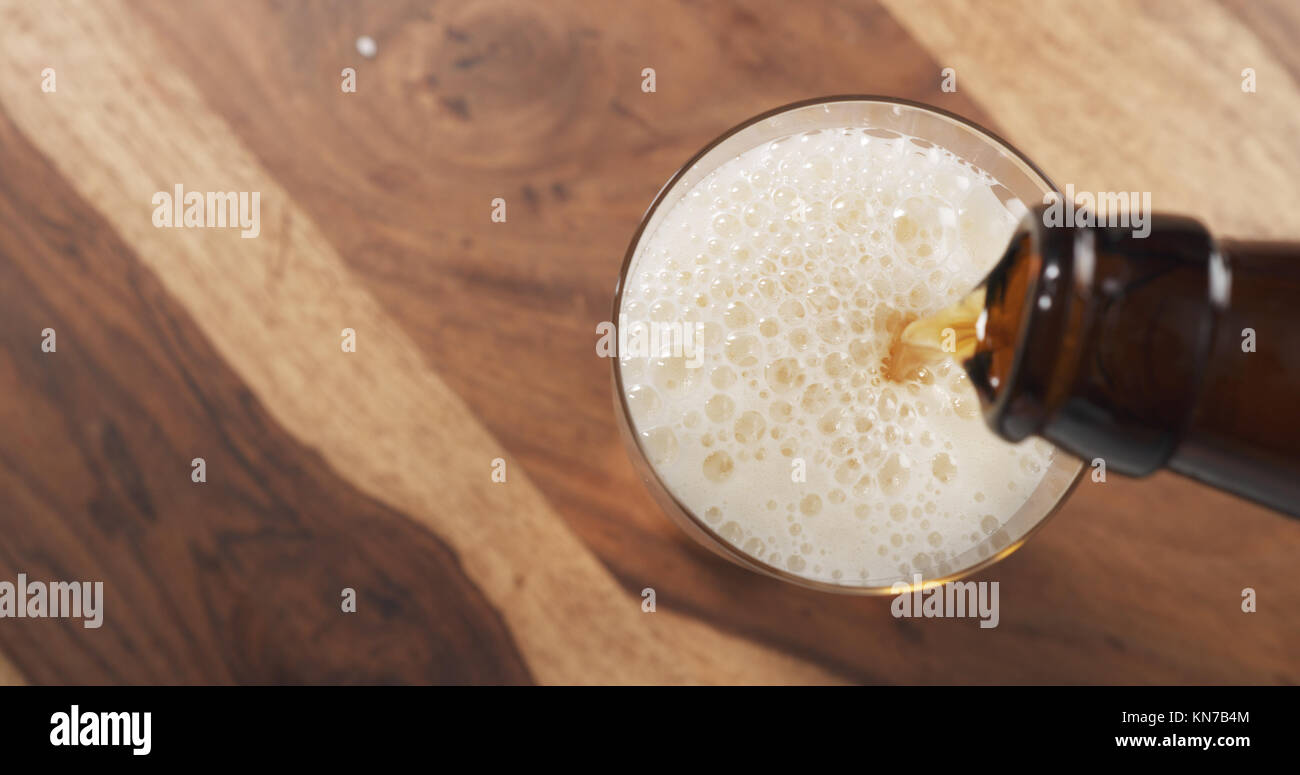 top view pouring lager beer from bottle into glass on wood table, wide ...