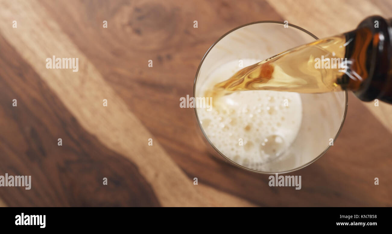 top view pouring lager beer from bottle into glass on wood table, wide ...