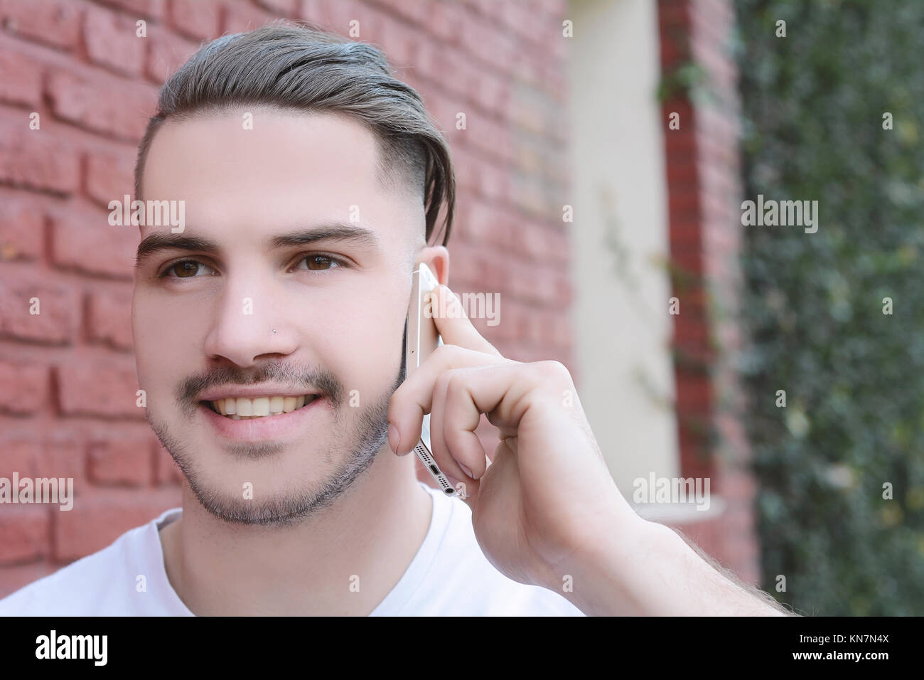 Portrait of young latin man talking on the phone against brick wall ...