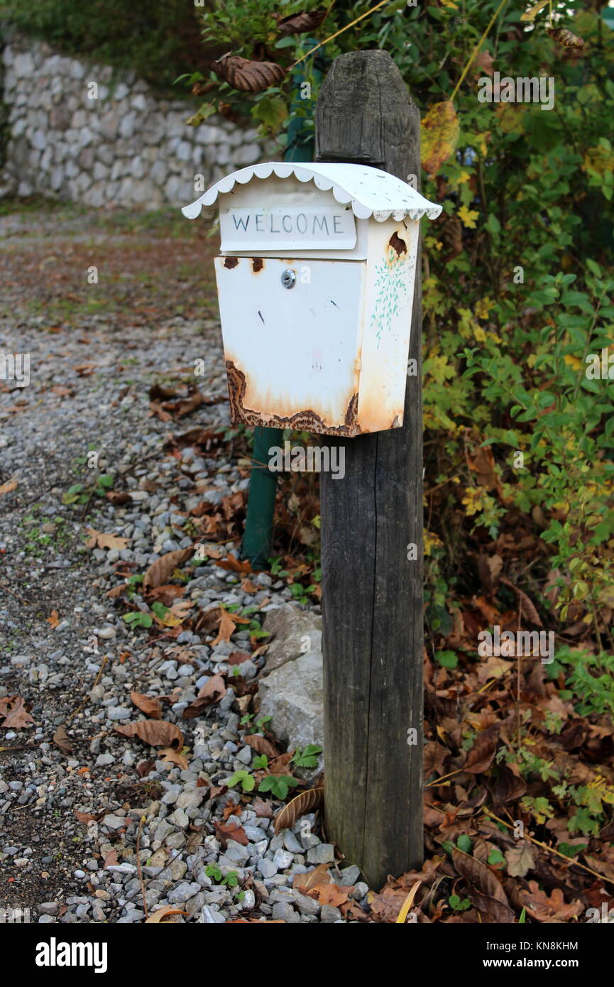 Rusted white mailbox with welcome sign mounted on old wooden pole next ...