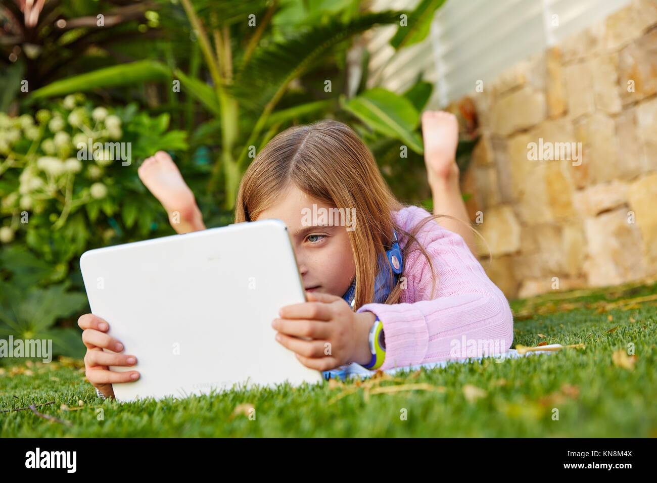 Blond kid girl with tablet pc lying on grass turf barefoot Stock Photo ...