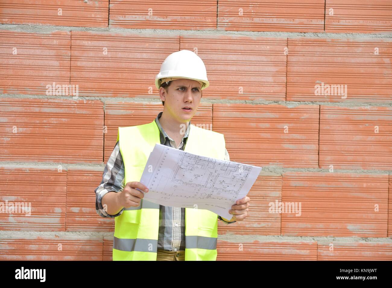 One engineer builder in front of orange brick wall with plan at ...