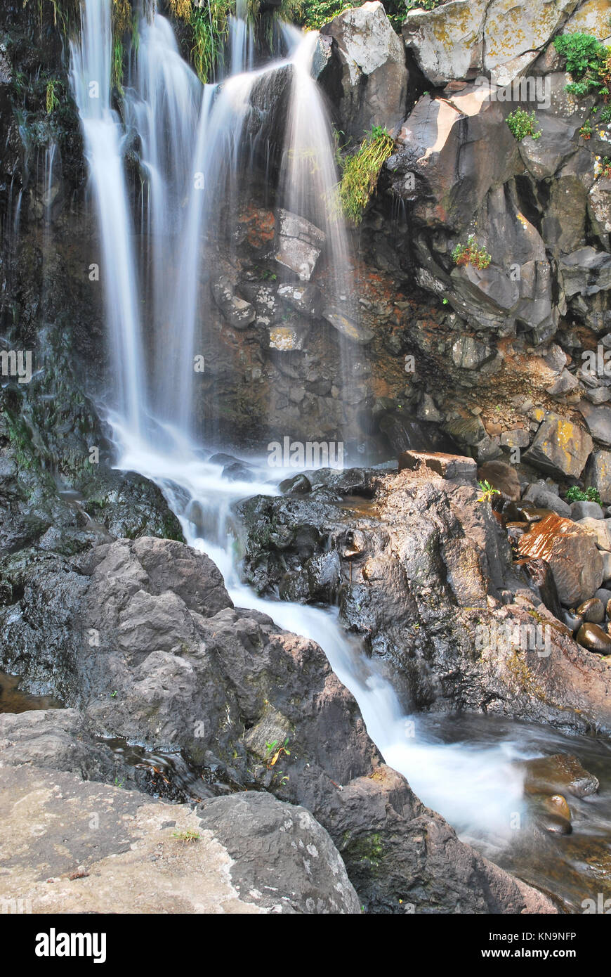 Low shot of majestic waterfall thundering down into a creek from a high ...