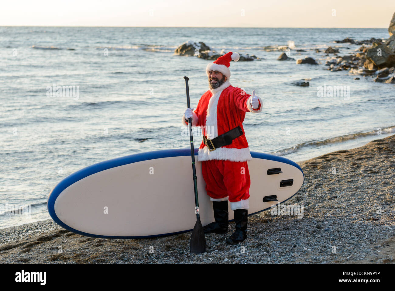 Man in Santa costume with SUP board on winter sea Stock Photo - Alamy