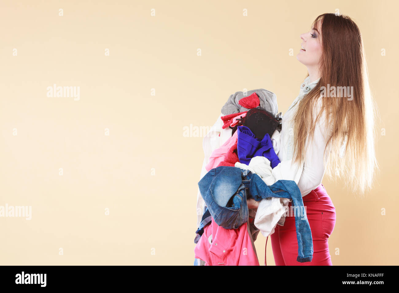 Young woman carrying stack pile of dirty laundry clothes. Girl cleaning tidying in studio ...