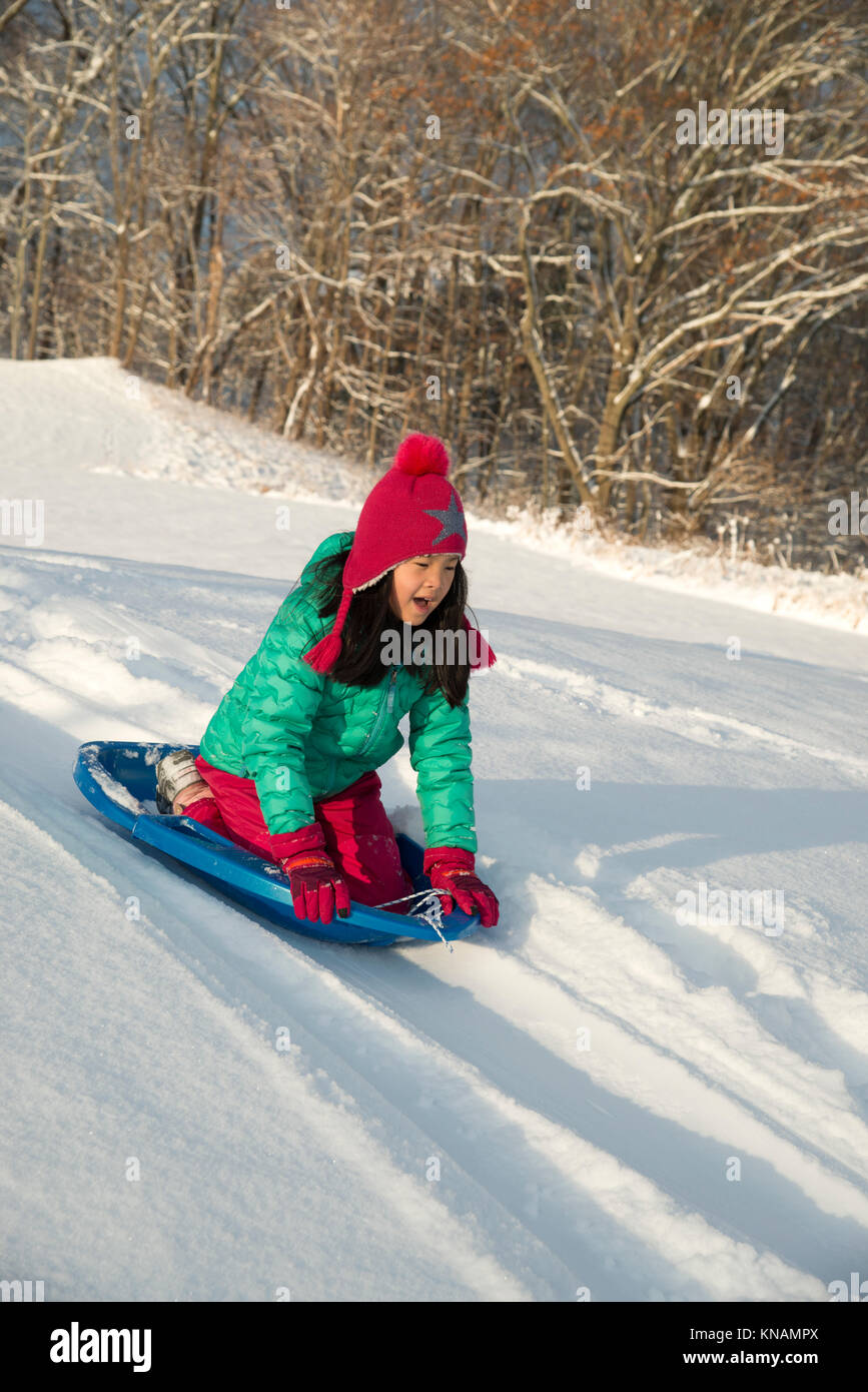 Happy young girl sledding down a snow covered hill in rural New ...
