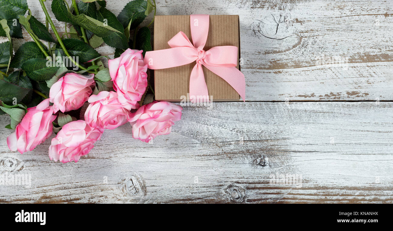 Half a dozen pink roses and gift box on rustic white wood in flat lay ...