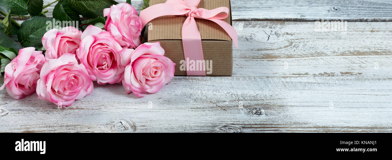 Front view of a half a dozen pink roses and gift box on rustic white ...