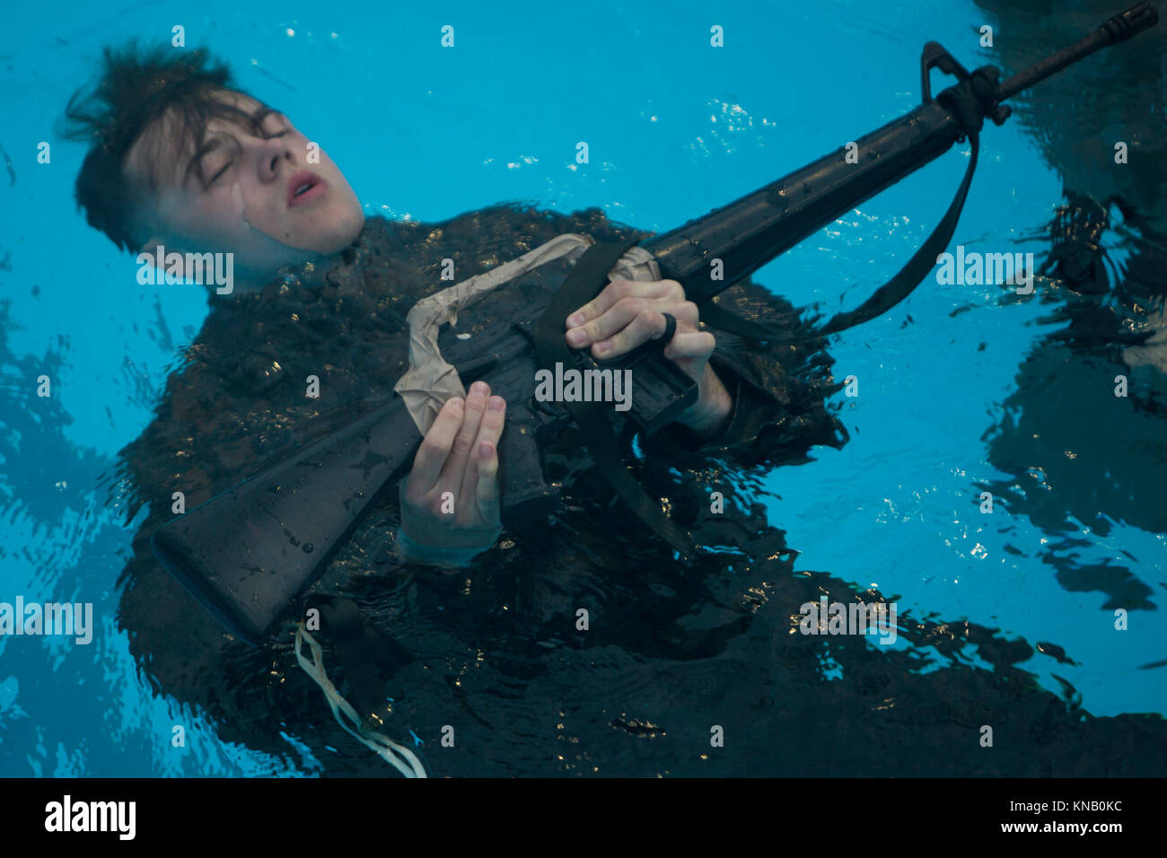 A Sailor carries a rifle during the water tread portion of a ...