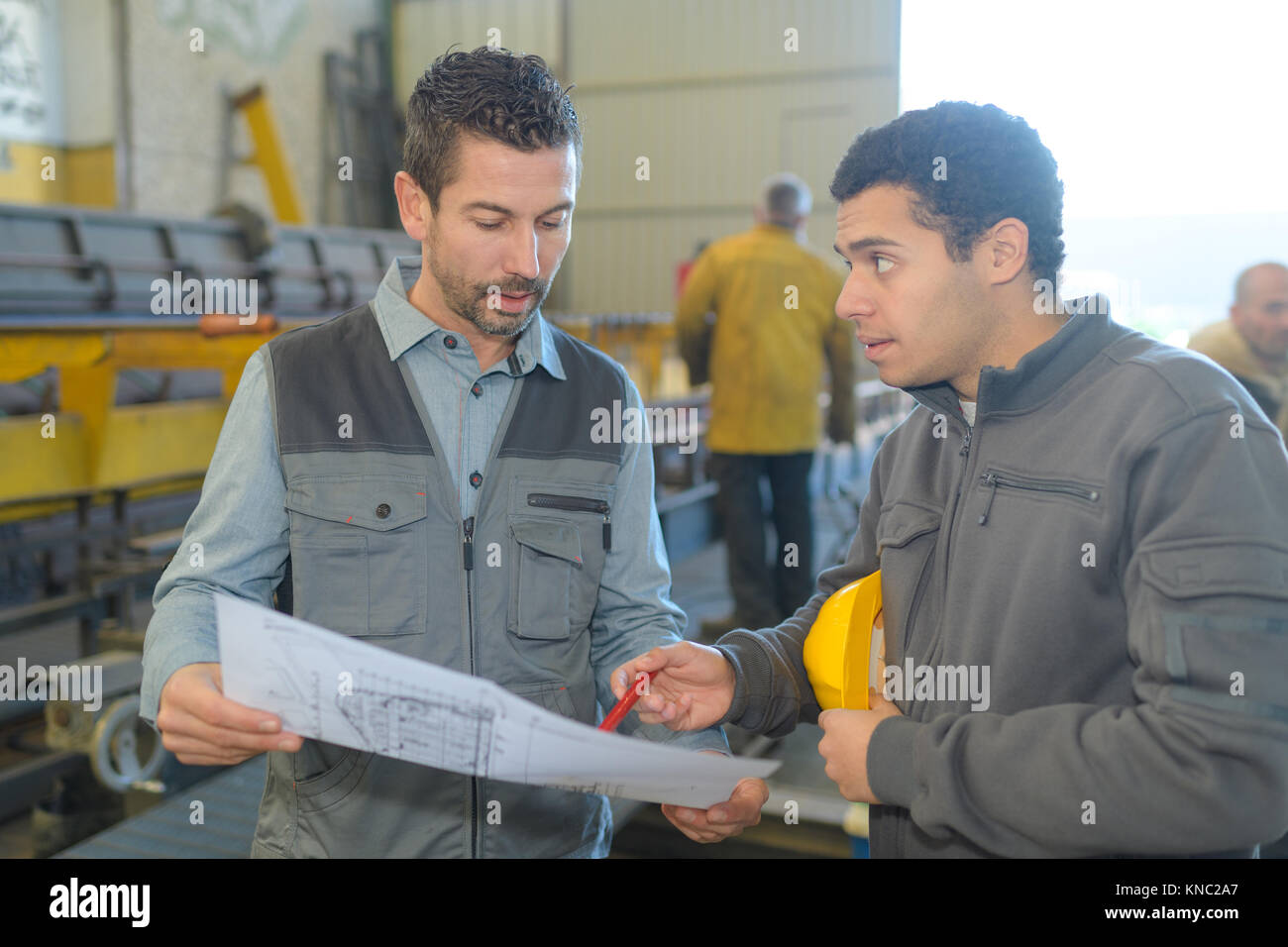 male supervisor with worker discussing over blueprints in industry ...