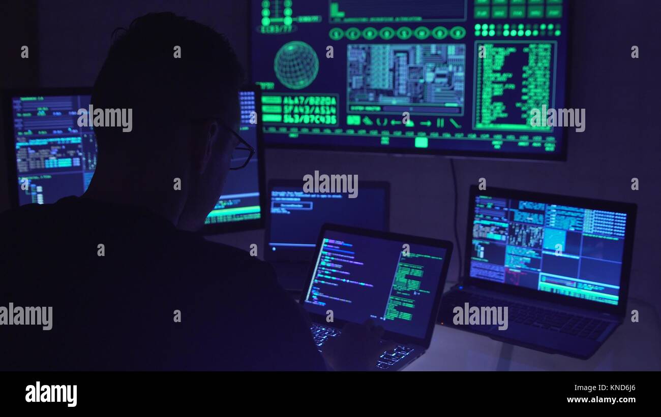 Male hacker working on a computer in a dark office room Stock Photo - Alamy
