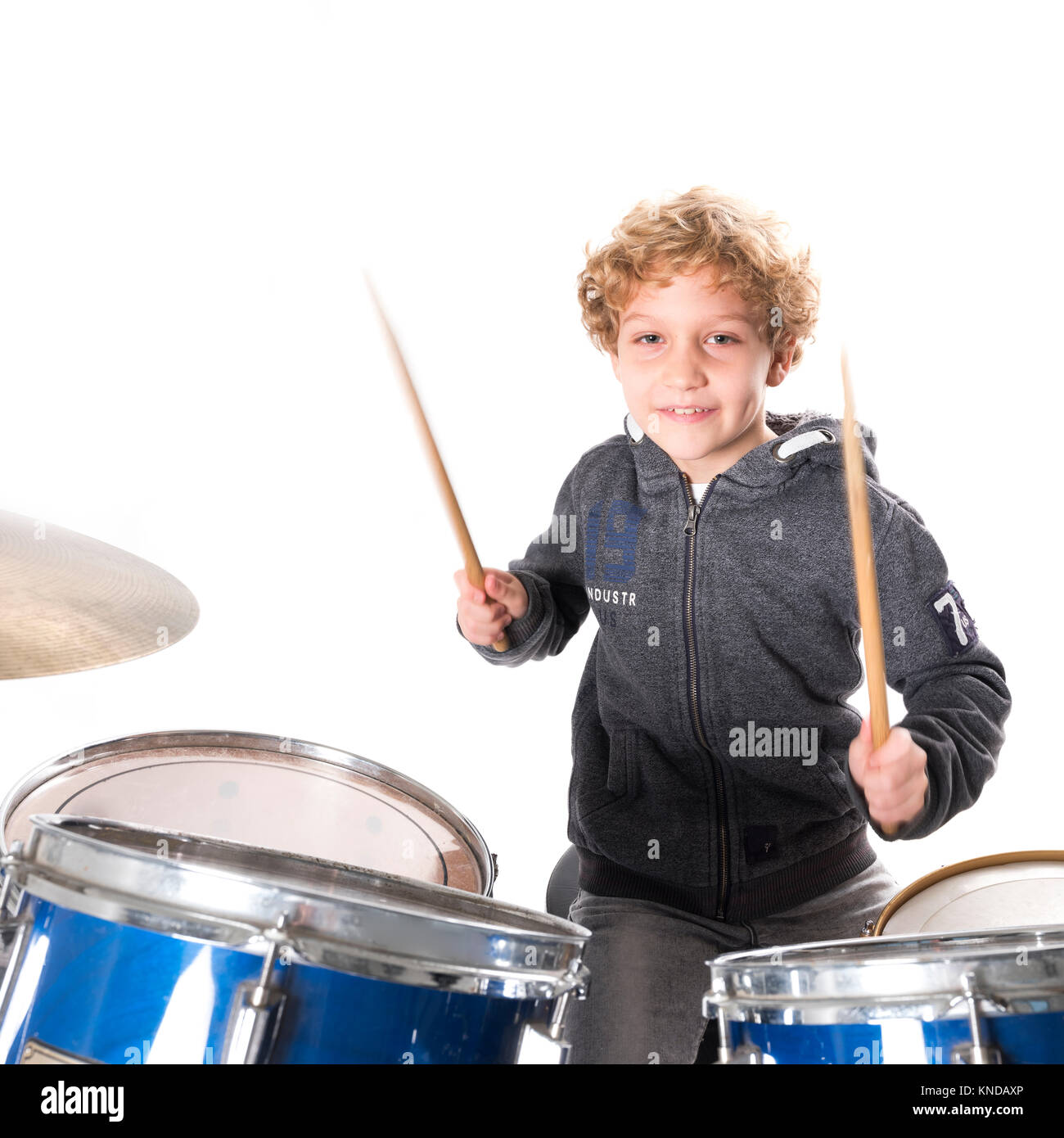 young blond caucasian boy at plays drums in studio against white ...