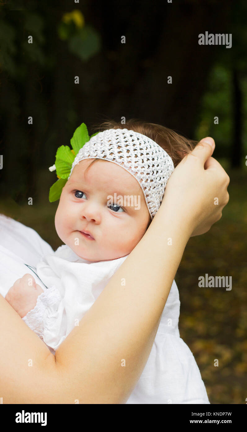 Mom's hand hugs little girl in white dress and with knitted headband ...