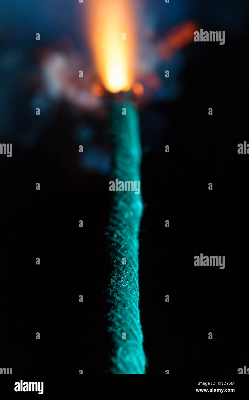 Close-up of burning fuse with sparks and blue smoke on black background ...