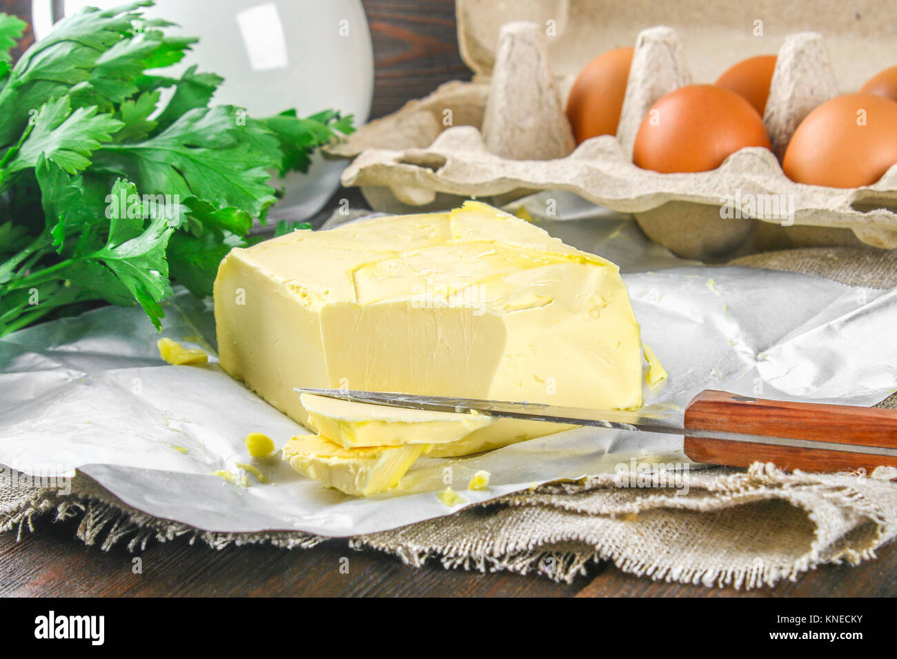 A bar of butter is cut into pieces on a wooden board with a knife ...