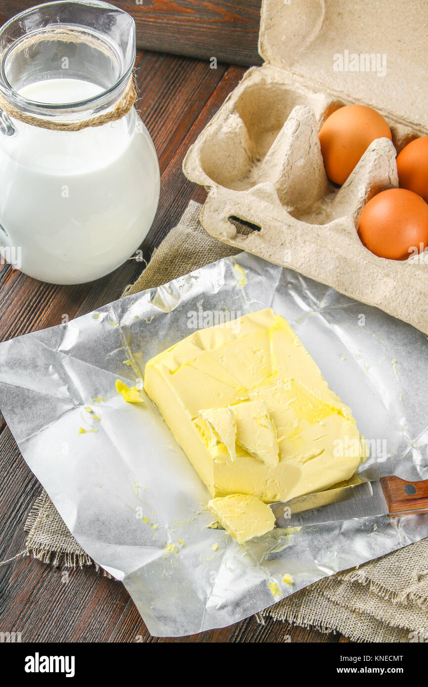A bar of butter is cut into pieces on a wooden board with a knife ...