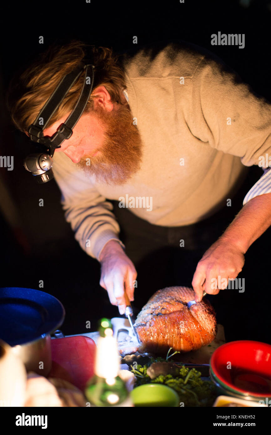 Man carving a roasted ham at night at a campsite Stock Photo - Alamy