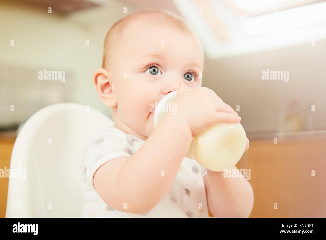 Baby boy sitting in high chair, drinking milk from bottle Stock Photo ...