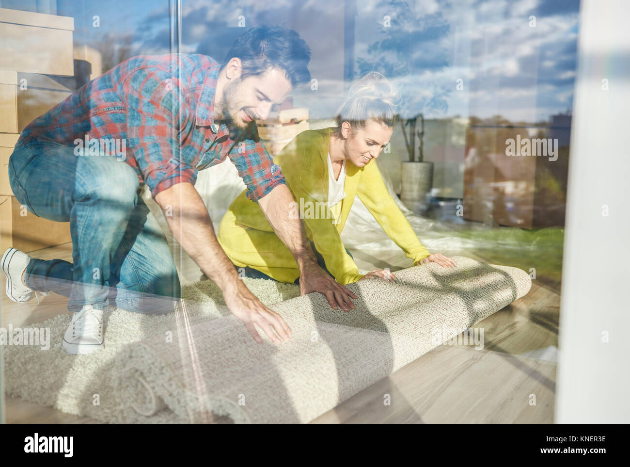 Young couple rolling out rug in new home, view through window Stock ...