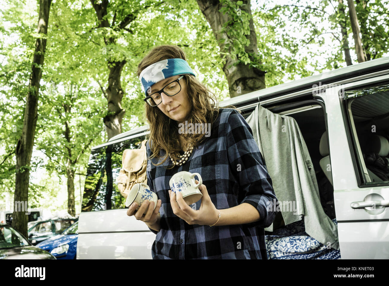 Female stall holder looking at second hand cups on stall at forest flea ...