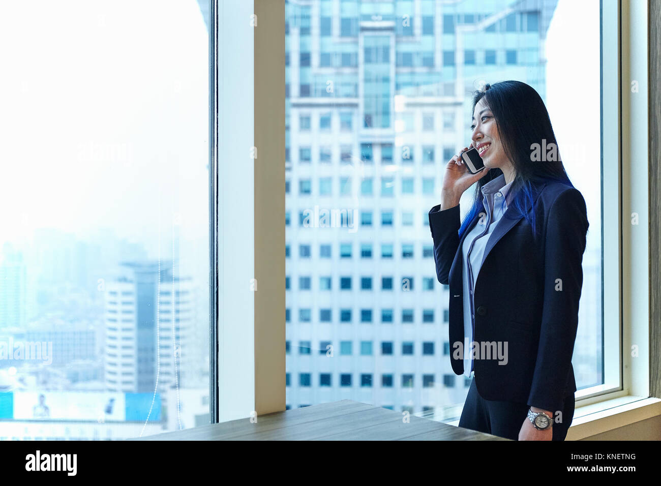 Businesswoman looking through window using smartphone to make telephone ...