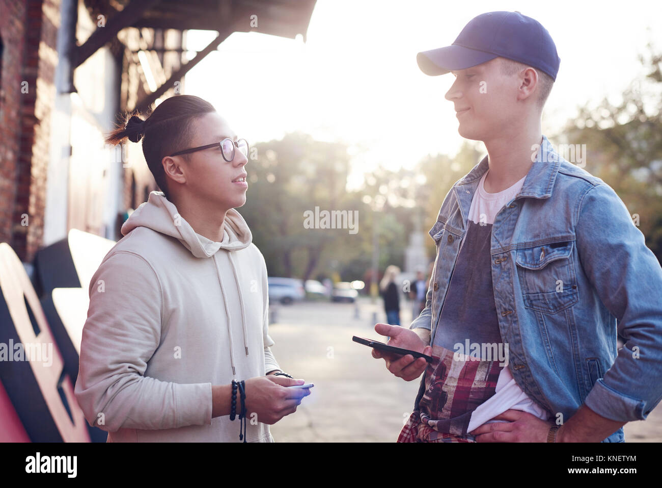 Two young men on city street chatting Stock Photo - Alamy