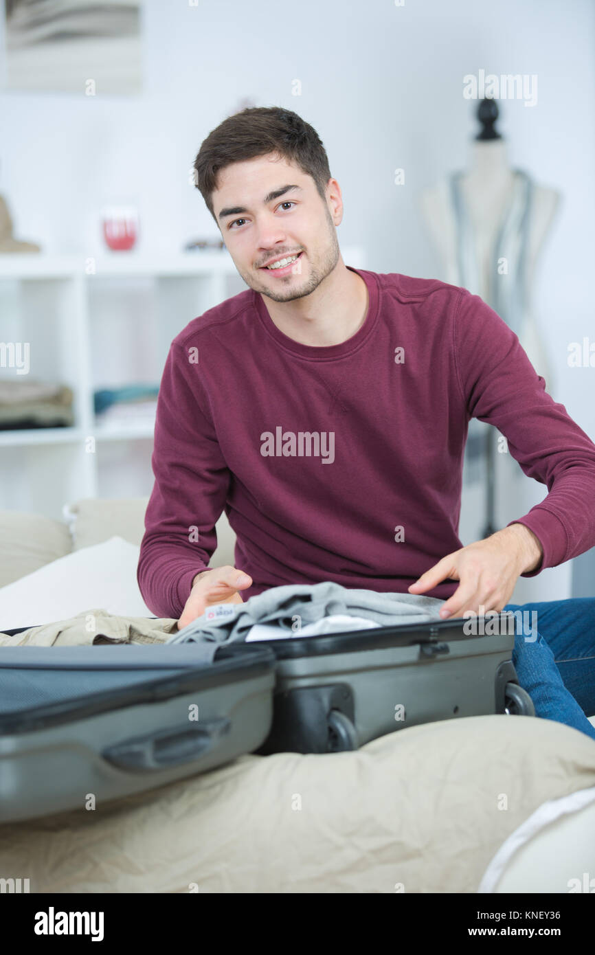 Young man packing clothes into suitcase Stock Photo - Alamy