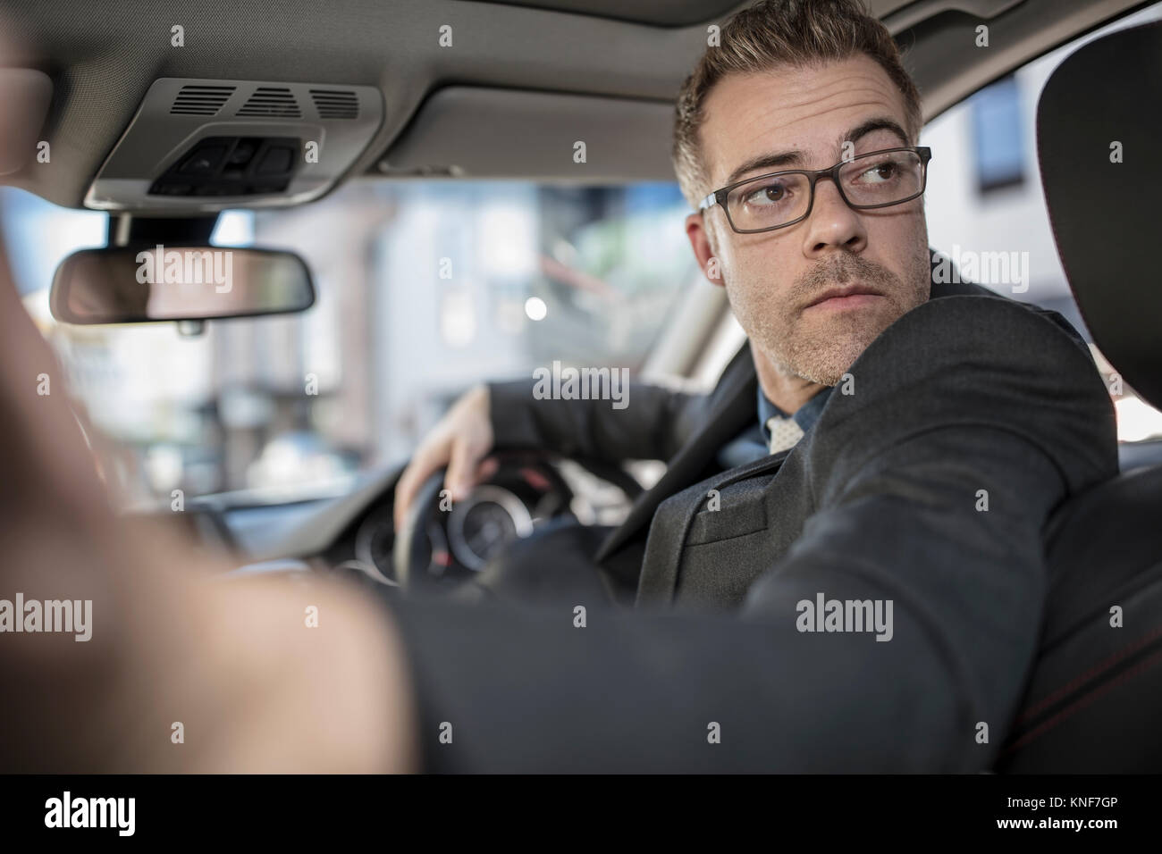 Businessman driving car, looking over shoulder, reversing Stock Photo ...