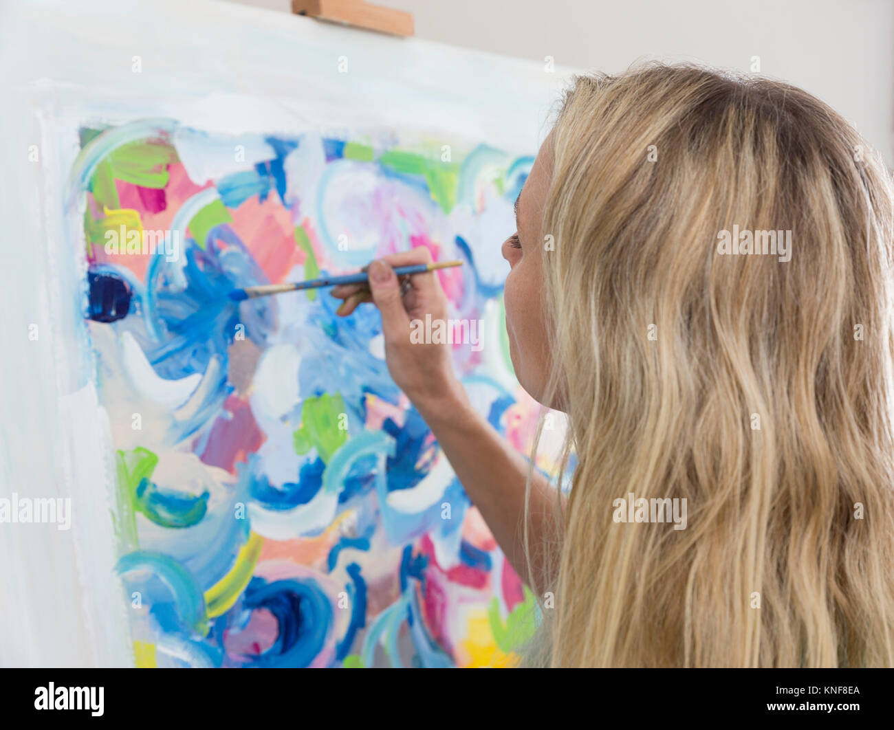Over shoulder view of female artist painting abstract canvas in studio ...