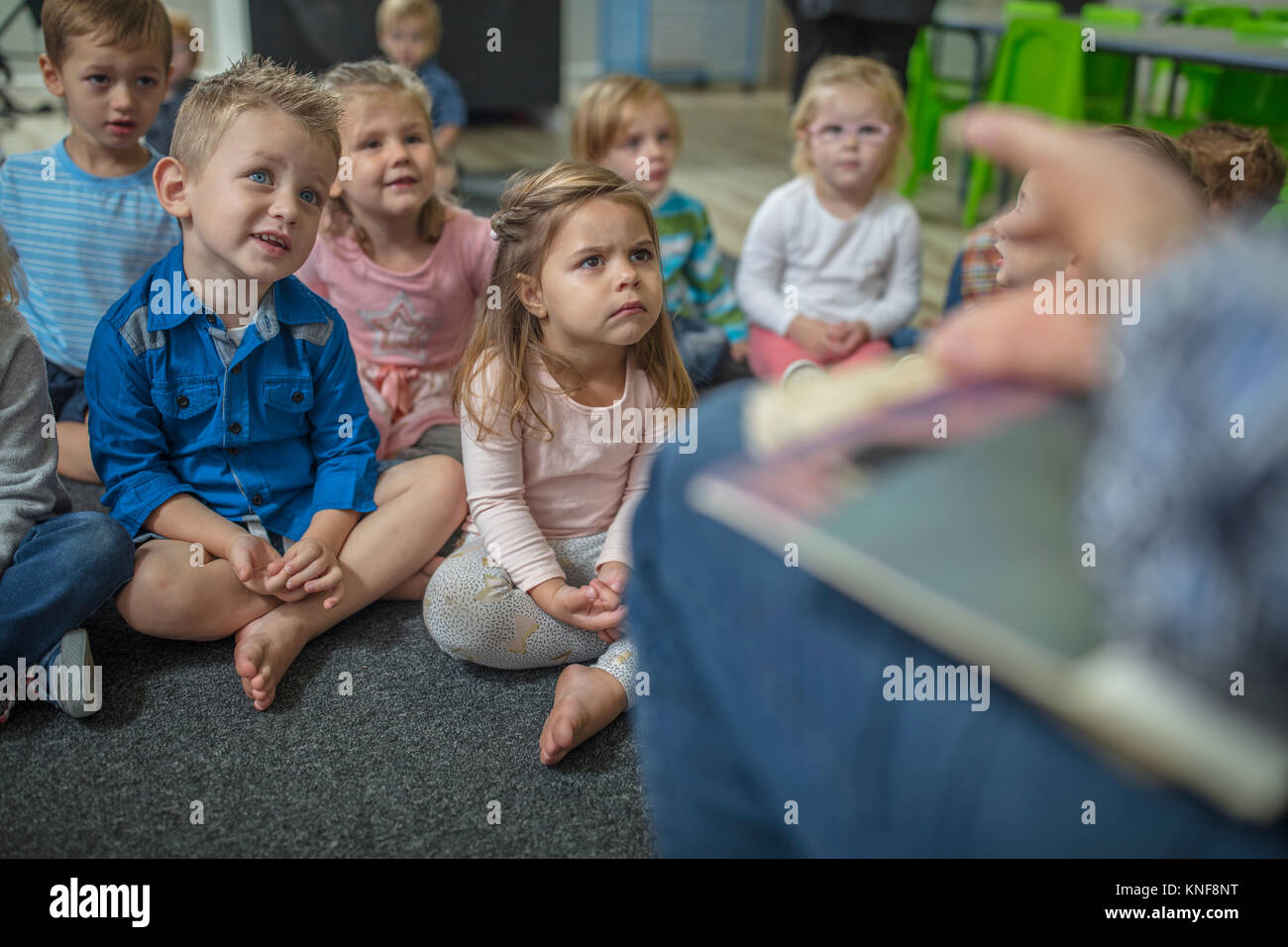 Young children sitting on carpet in classroom, listening to teacher at ...