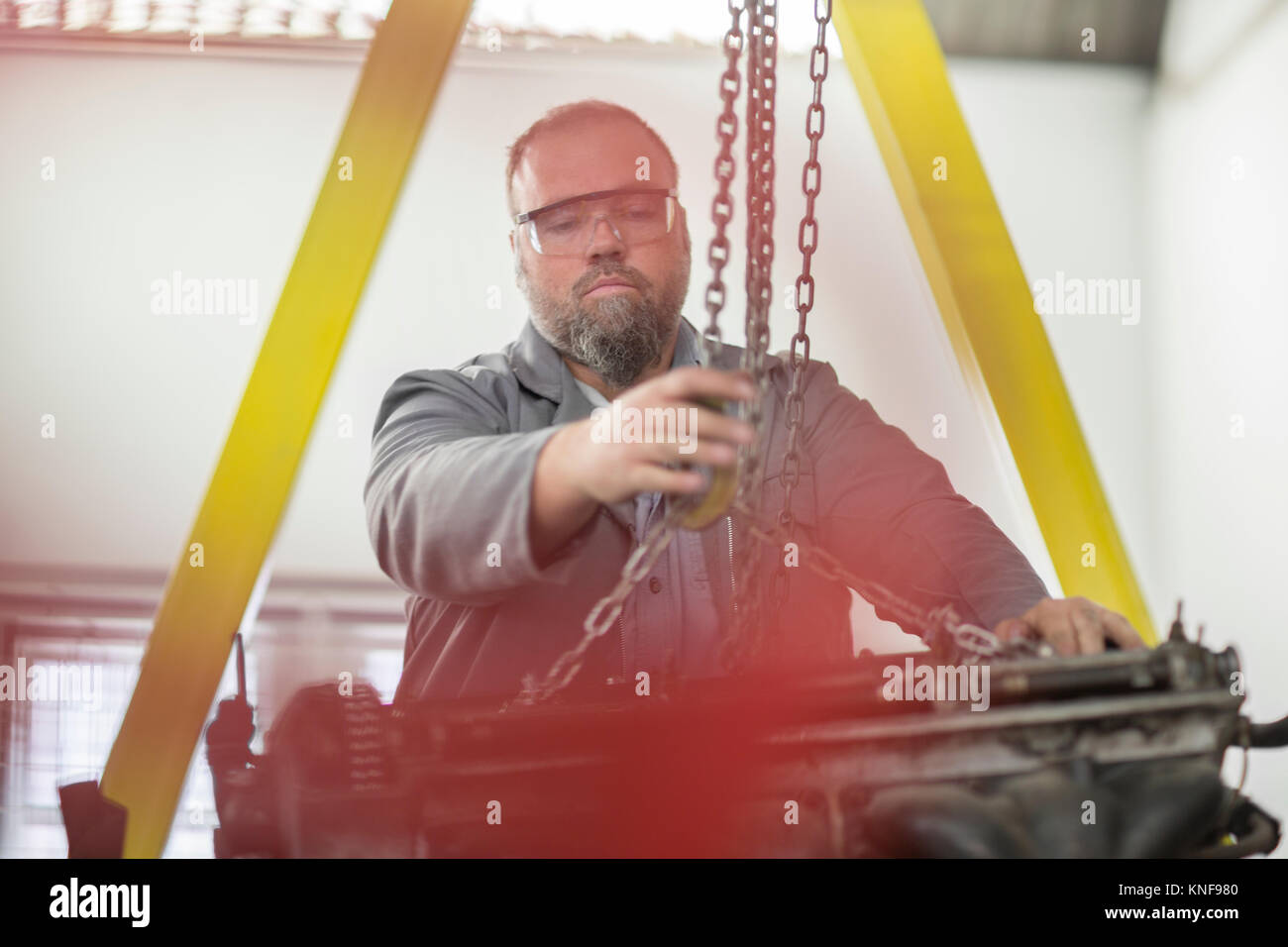 Male car mechanic attaching hoist chain to car engine in repair garage ...