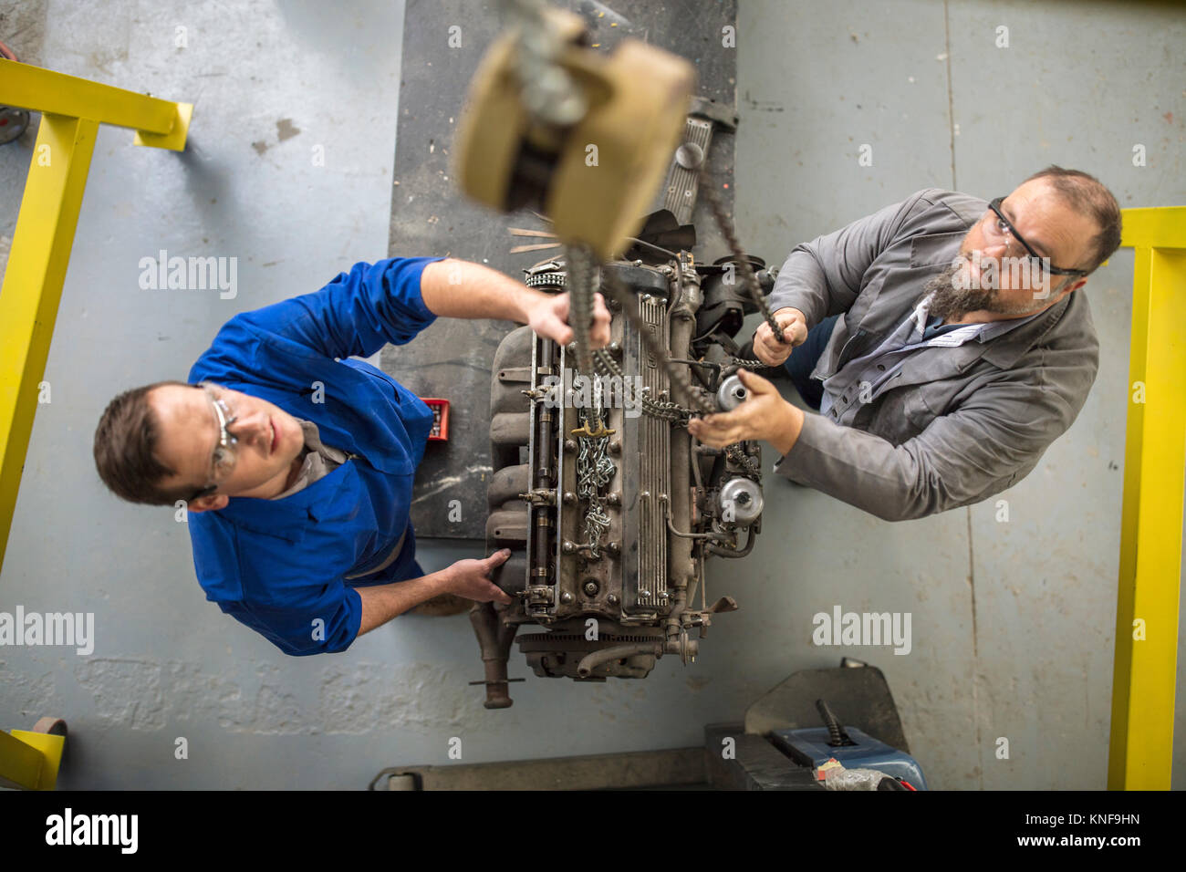 Overhead view of car mechanics hoisting car engine in repair garage ...