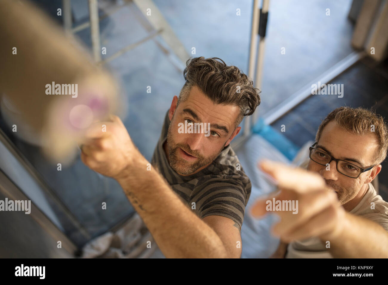 Man painting wall using paint roller, male friend pointing to area ...
