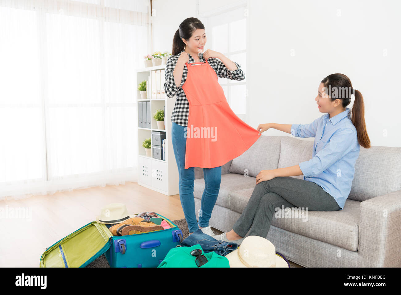 young beautiful girl packing luggage at home with sister and showing ...