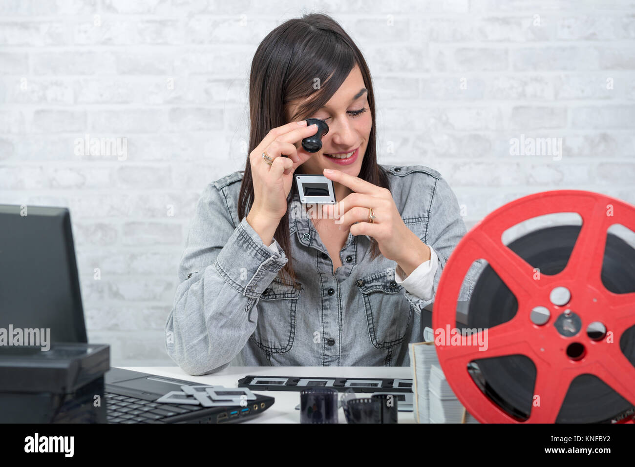 young brunette woman looking at film slide with a magnifying glass ...