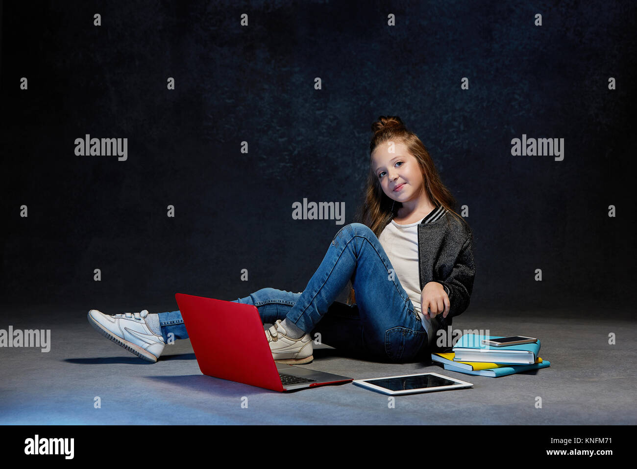 Little girl sitting with laptop, tablet and phone in gray studio Stock ...