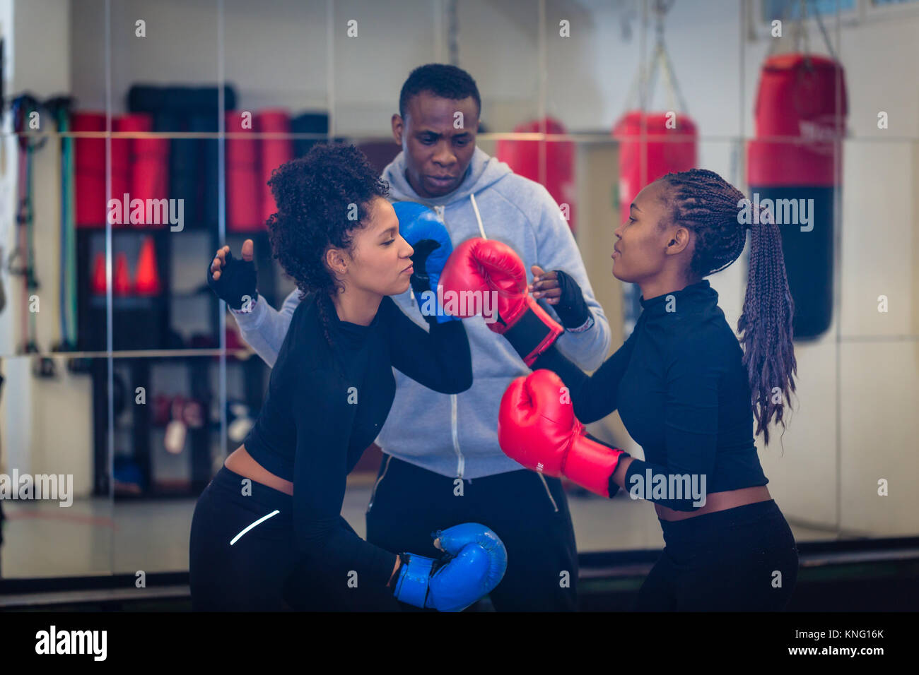 Experienced boxing trainer supervising and teaching two female b Stock ...