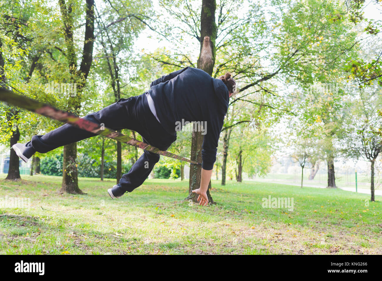 Man balancing a tightrope or slackline outdoor in a city park in autumn ...