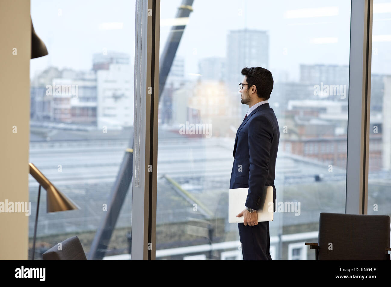 Caucasian businessman standing alone looking out of an office window at ...
