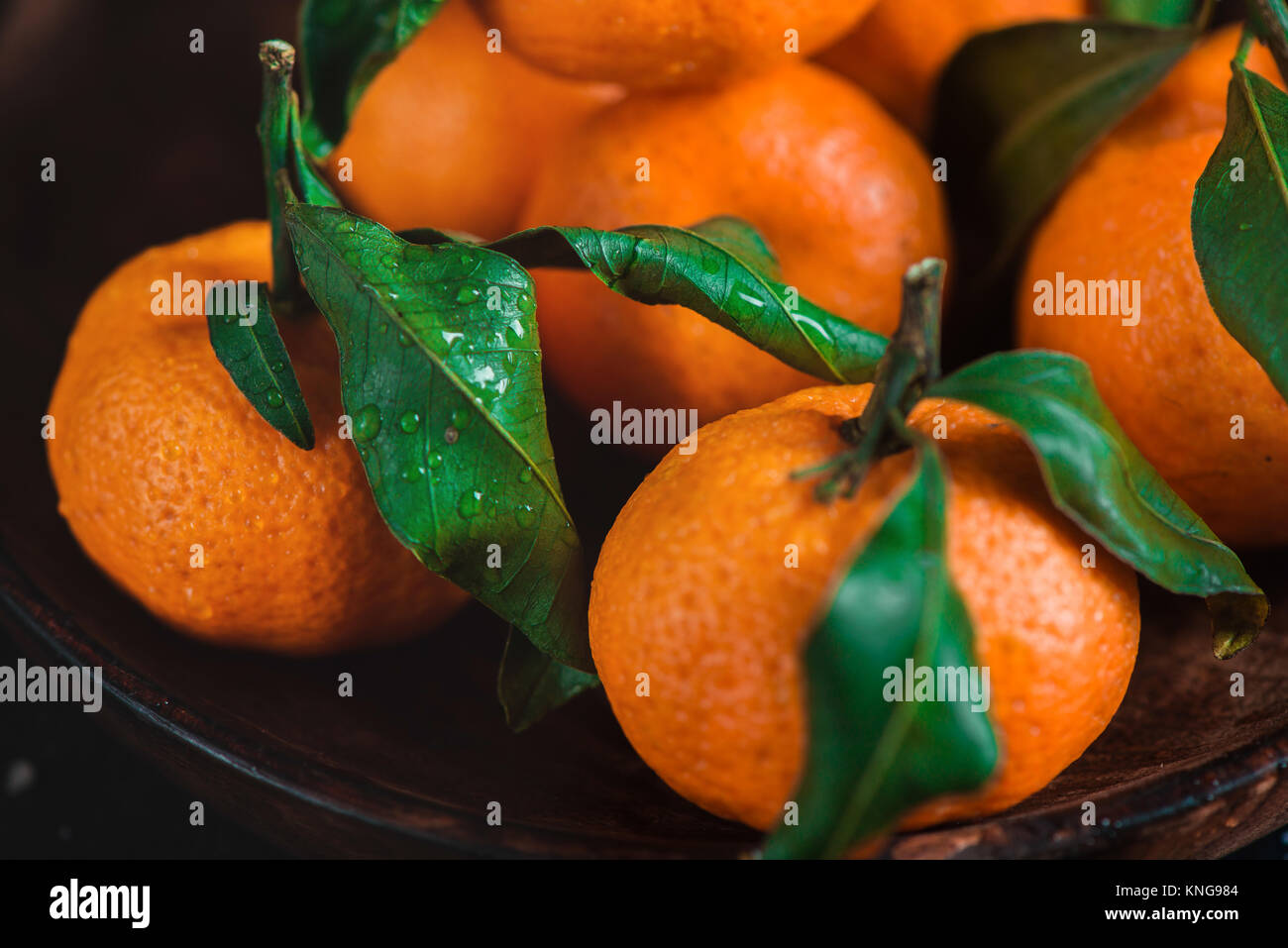 Close-up of tangerines in a wooden plate on a dark background. Water ...