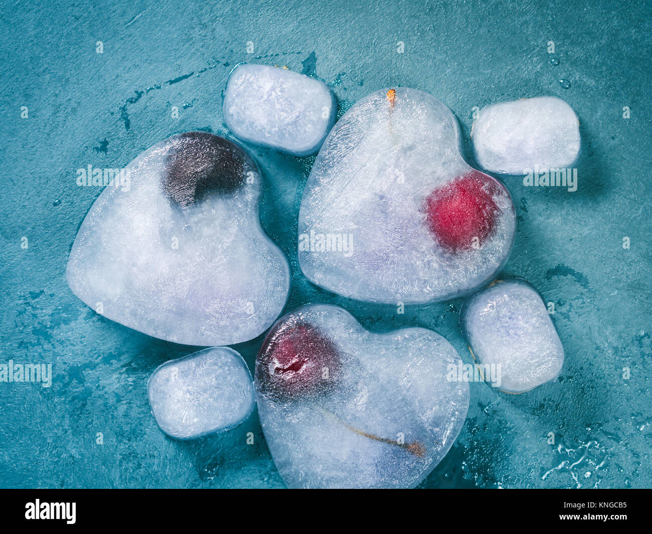 Heart shaped lavender syrup ice cubes with frozen cherry on blue ...